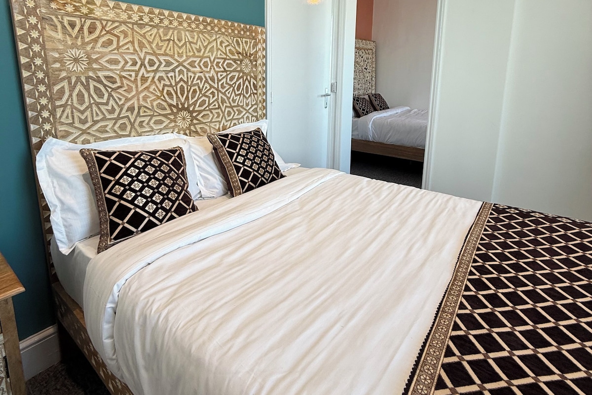 Quarto com cabeceira estampada, cama com roupa de cama branca e tapete estampado.