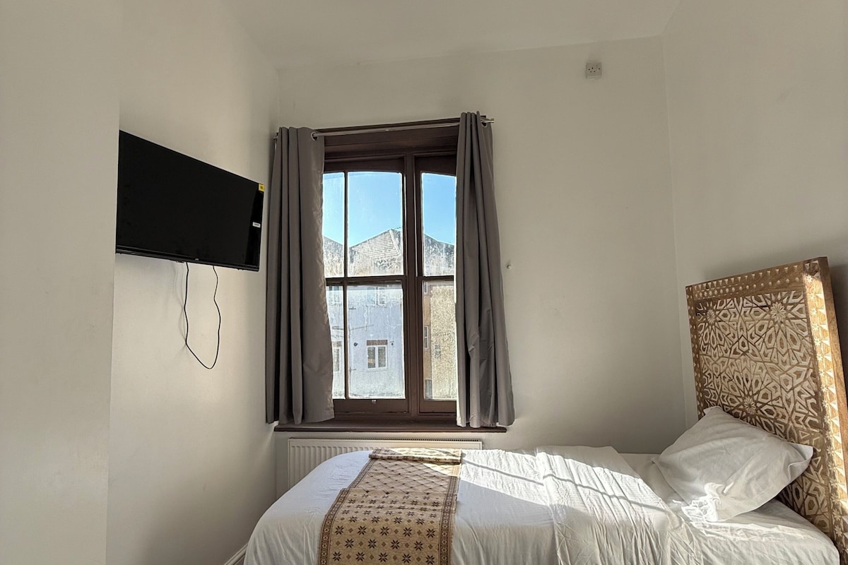 Quarto com cama, janela com cortinas, TV de tela plana na parede e luminária.