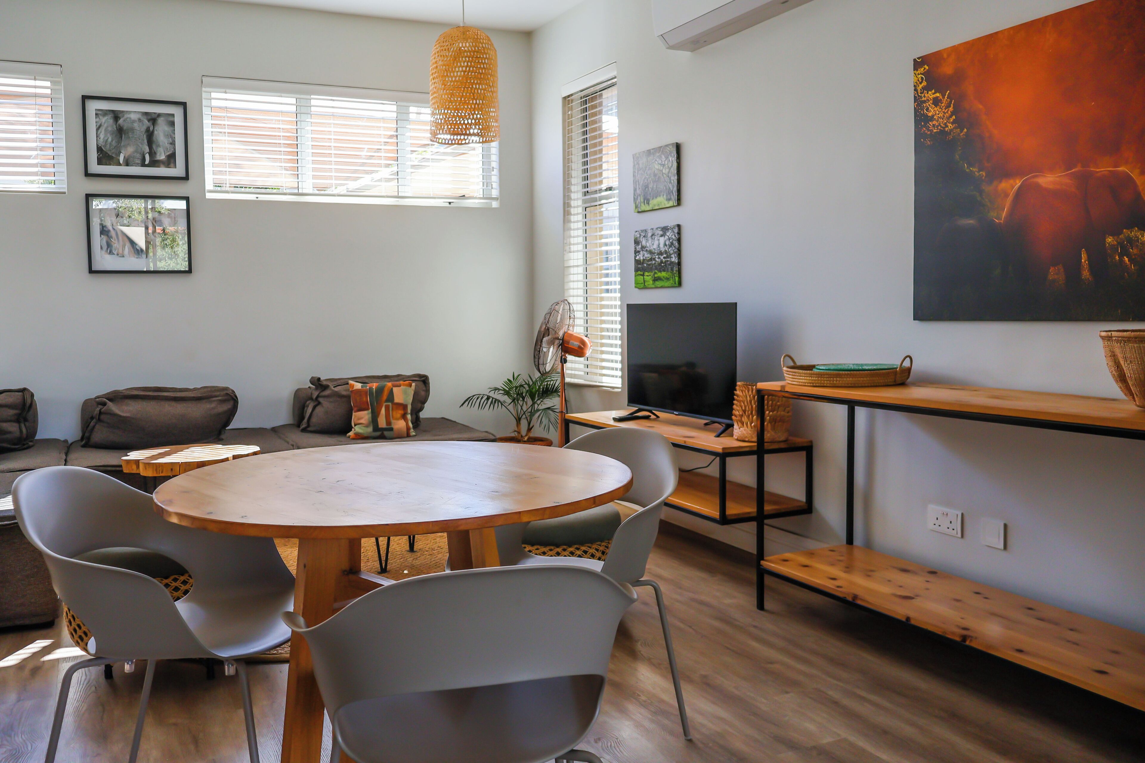 A modern living room with a round wooden table, grey chairs, a sofa, a TV, and artwork on the walls.