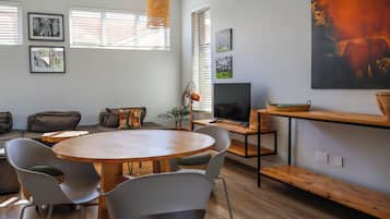 A modern living room with a round wooden table, grey chairs, a sofa, a TV, and artwork on the walls.
