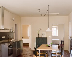 Cozinha moderna com área de jantar, apresentando uma mesa e cadeiras de madeira, luminária pendente e vista para outro cômodo.