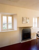 Um quarto com lareira, duas janelas e uma porta.