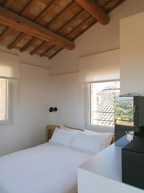 Quarto com cama, mesa de cabeceira, janela e vista exterior.