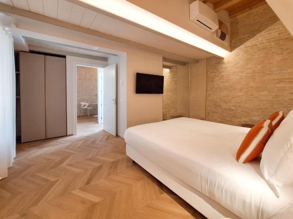 Quarto com cama, televisão e chão de madeira.
