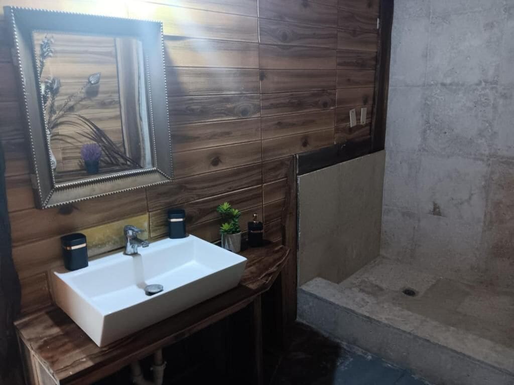 A bathroom with a wooden vanity, a white sink, a mirror, and a shower area.