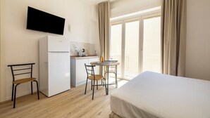 Quarto de hotel com cama, escrivaninha, cadeira, televisão e varanda com cortinas.