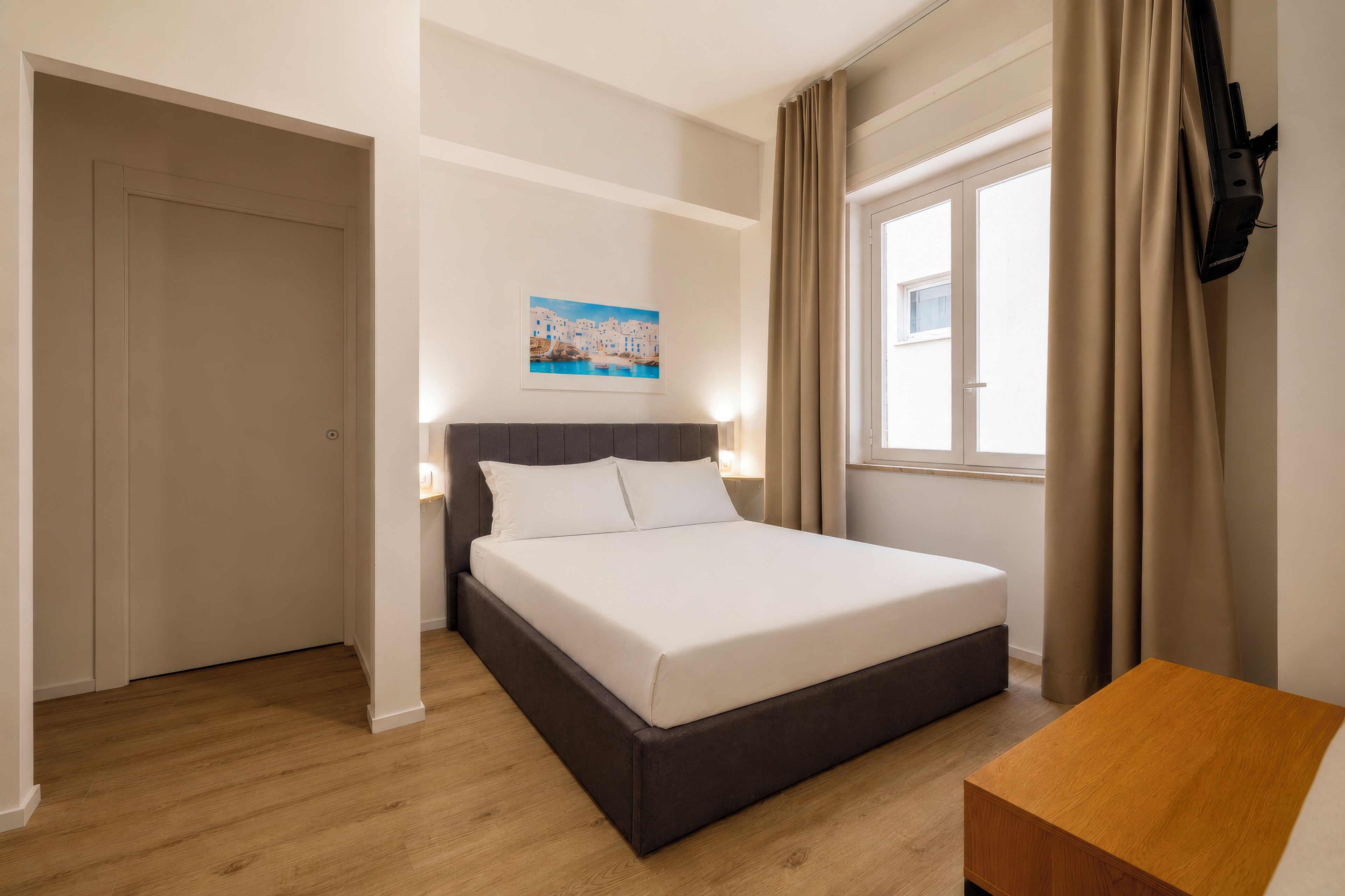 Quarto com cama, mesa de cabeceira, janela com cortinas e um quadro na parede.