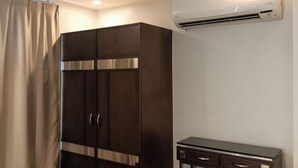 Quarto com guarda-roupa escuro, pequena escrivaninha e ar condicionado.
