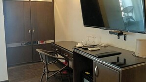 Quarto de hotel compacto com escrivaninha, cadeira, televisão e guarda-roupa.