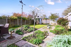 Um jardim com mesa e cadeiras no alpendre, um pequeno galpão e uma cerca.