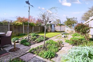 Um jardim com mesa e cadeiras no alpendre, um pequeno galpão e uma cerca.