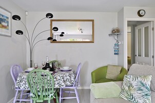 Uma sala de jantar com uma mesa posta para dois, uma poltrona verde e um sofá com almofadas estampadas.