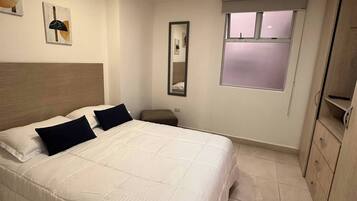 Um quarto com uma cama, mesa de cabeceira, espelho, janela e guarda-roupa.