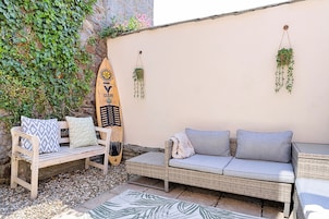 Uma área de estar ao ar livre aconchegante, com um banco de madeira, um sofá de vime e uma decoração com prancha de surf.