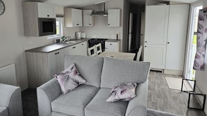 Um espaço compacto com cozinha americana, sofá cinza com almofadas estampadas e vista para o exterior.