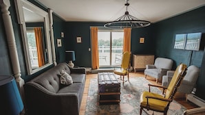 A living room with a sofa, armchairs, a table, a lamp, and a large window with curtains.