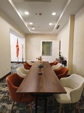 Uma sala de conferência com uma mesa comprida e várias cadeiras, uma bandeira e uma janela.
