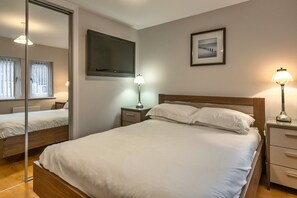 Quarto de hotel com cama, mesas de cabeceira, abajur, espelho e quadro na parede.