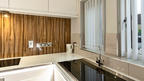 Uma cozinha moderna com painel de madeira na parede, eletrodomésticos de aço inoxidável e uma janela com persianas.