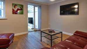 Uma sala de estar com uma mesa de centro de vidro, um sofá de couro vermelho, uma TV de tela plana na parede e um quadro na parede.