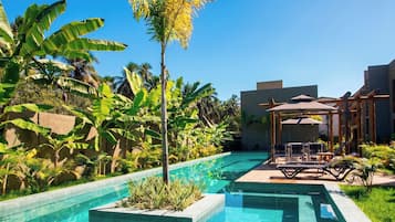 Uma área de piscina com pergolado, espreguiçadeiras e vegetação tropical.