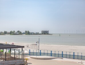 Uma praia com uma cerca azul, um edifício e turbinas eólicas ao longe.