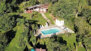 Vista aérea de uma propriedade com piscina, varanda coberta e um pequeno edifício.