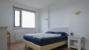 Quarto com cama, mesa de cabeceira, radiador, janela e luminária na parede.
