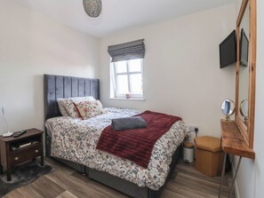 Um quarto com cama, mesa de cabeceira, janela e espelho.