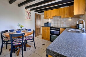 Cozinha com armários de madeira, micro-ondas, forno e mesa de jantar com cadeiras.