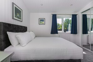 Quarto com cama, mesa de cabeceira, quadro pendurado na parede e janela com cortinas.