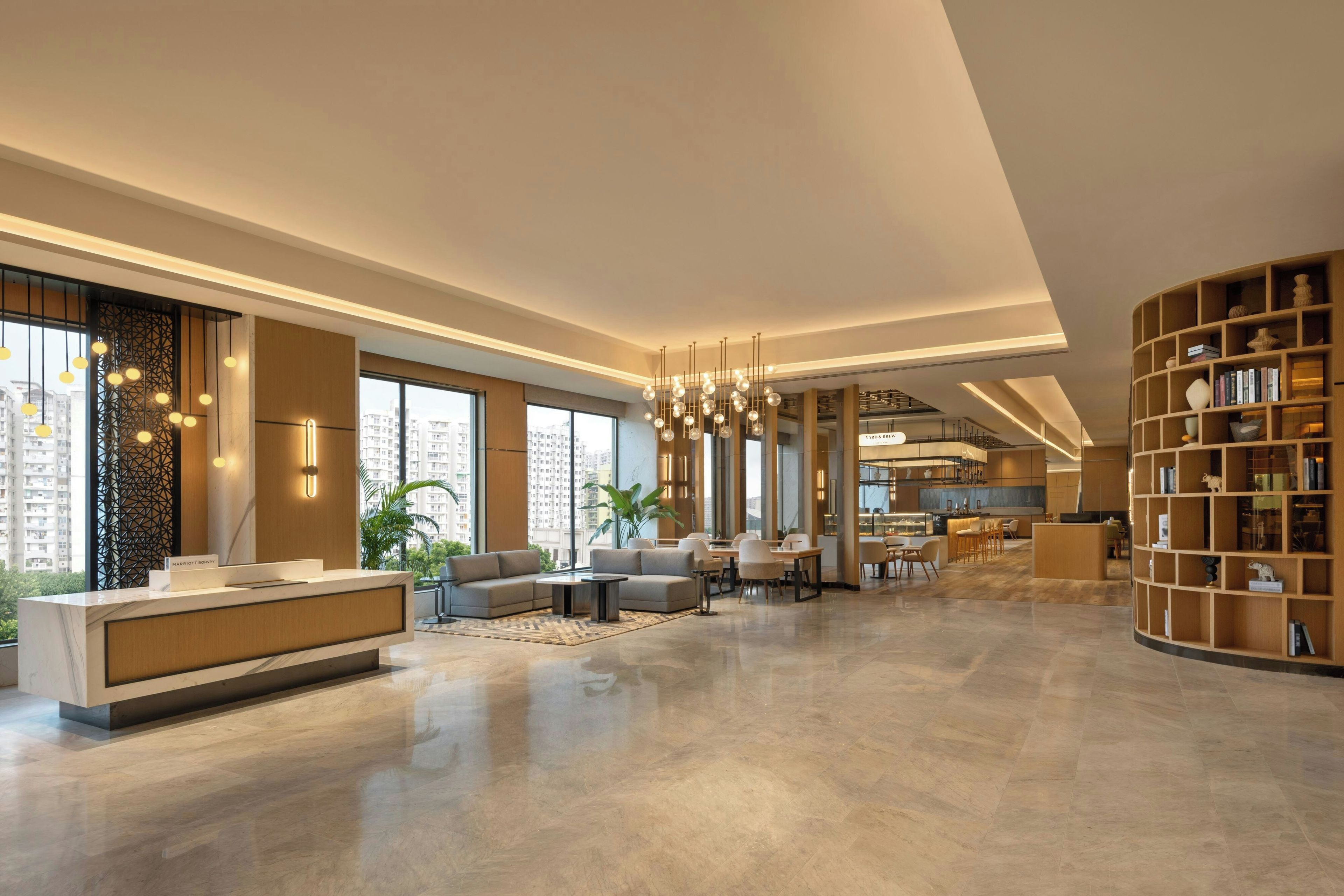 Um hall de hotel moderno com balcão de recepção, área de estar e cozinha visível ao fundo.