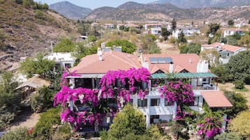 Um edifício residencial com telhado de telhas vermelhas, rodeado por vegetação exuberante e plantas floridas.