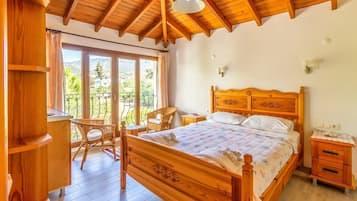 Quarto com estrutura de madeira, cama, mesas de cabeceira e varanda com móveis de vime.