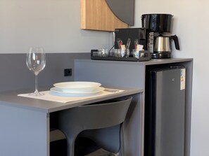 Uma cozinha compacta com cafeteira, geladeira, um copo de vinho e um prato sobre a mesa.