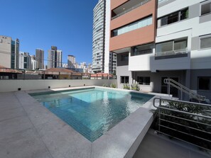 Piscina no terraço com vista para a cidade, rodeada por edifícios modernos.