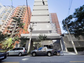 Edifício de vários andares com design moderno, destacando uma entrada imponente com porta de vidro e uma pequena cobertura.