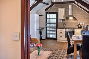 Uma cozinha moderna com forno embutido, área de jantar com mesa e cadeiras, e vista para a sala de estar através de uma porta de vidro.