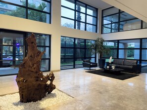 Um hall amplo com uma grande escultura de madeira, um sofá de couro preto e uma planta em vaso.