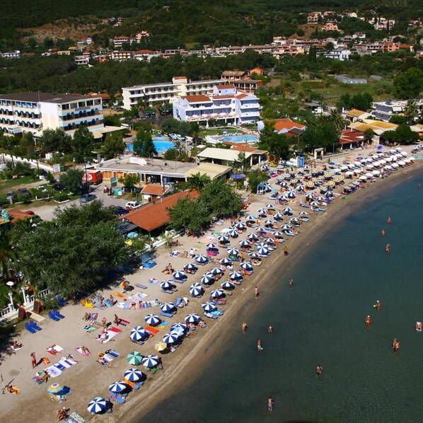 Um resort à beira-mar com extensa faixa de areia, vários guarda-sóis e área de piscina.