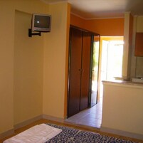 Quarto com cama, televisão fixada na parede, guarda-roupa e janela com luz natural.