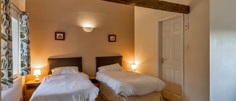 Quarto de hotel com duas camas, uma viga de madeira no teto, uma porta e duas luminárias fixadas na parede.