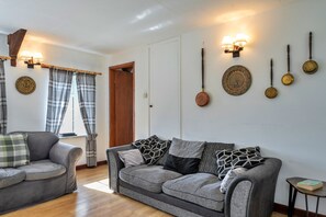 Uma sala de estar com sofá cinza, duas poltronas, cortinas xadrez, luminárias fixadas na parede e pratos decorativos.