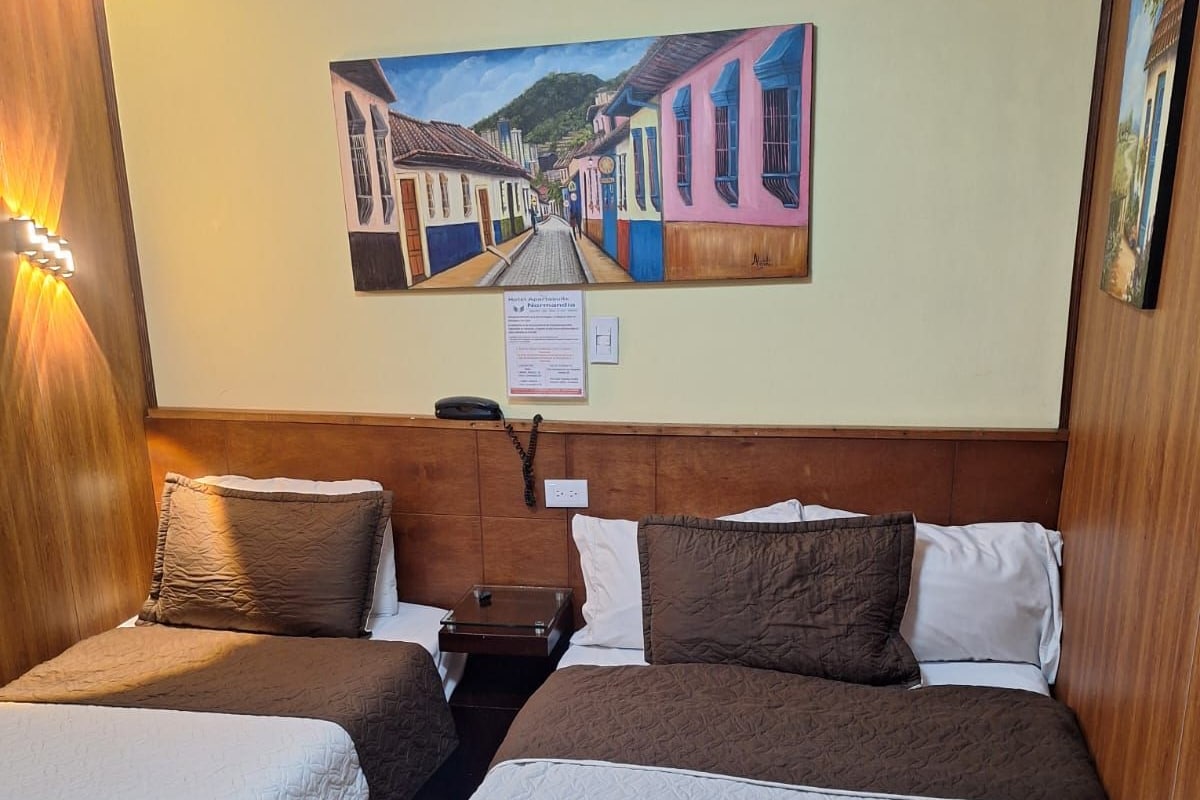 Quarto de hotel com duas camas, um quadro de uma cena urbana na parede e cabeceira de madeira.