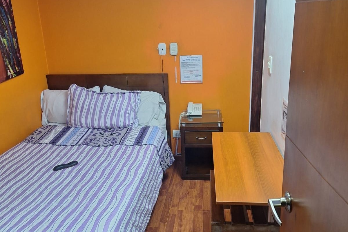 Quarto de hotel com cama, mesa de cabeceira e uma pequena mesa de madeira.