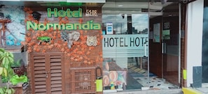 Entrada de hotel com uma placa indicando 'Hotel Normandía' e uma parede decorativa com diversas figuras de animais e folhas de outono.