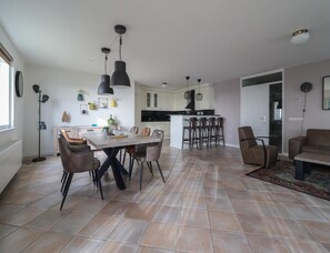 Uma cozinha moderna com armários brancos, uma sala de jantar com mesa e cadeiras, e uma sala de estar com sofá.