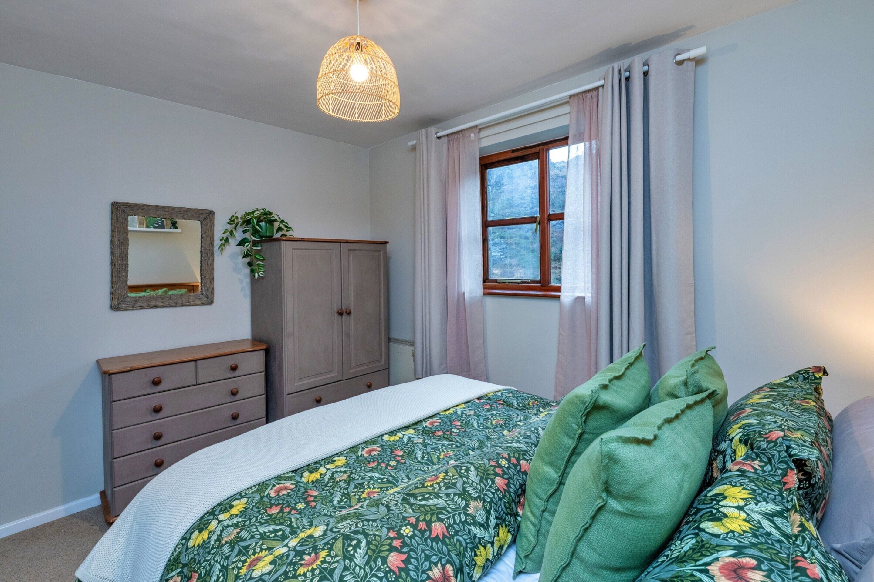 Quarto com cama, guarda-roupa, janela com cortinas e luminária pendente.