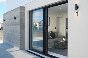Um edifício moderno com entrada por porta de vidro, fachada de concreto e interior visível, com um sofá e uma mesa de centro.