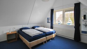 A bedroom with two beds, a window with curtains, a radiator, and a small bedside table with a lamp.